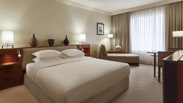 Quarto de hotel com uma cama grande, mesas de cabeceira, escrivaninha, cadeira e uma janela ampla com cortinas.