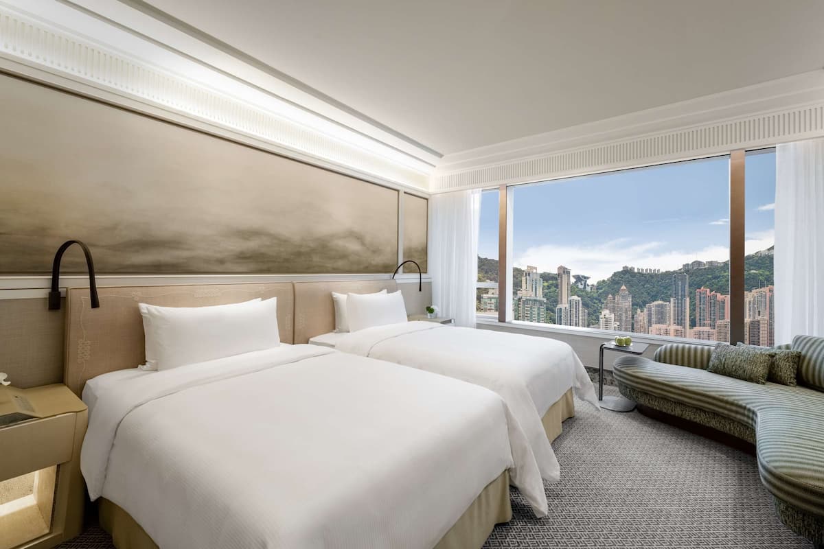Quarto de hotel com duas camas, um sofá, uma janela grande com vista para a cidade e design moderno.