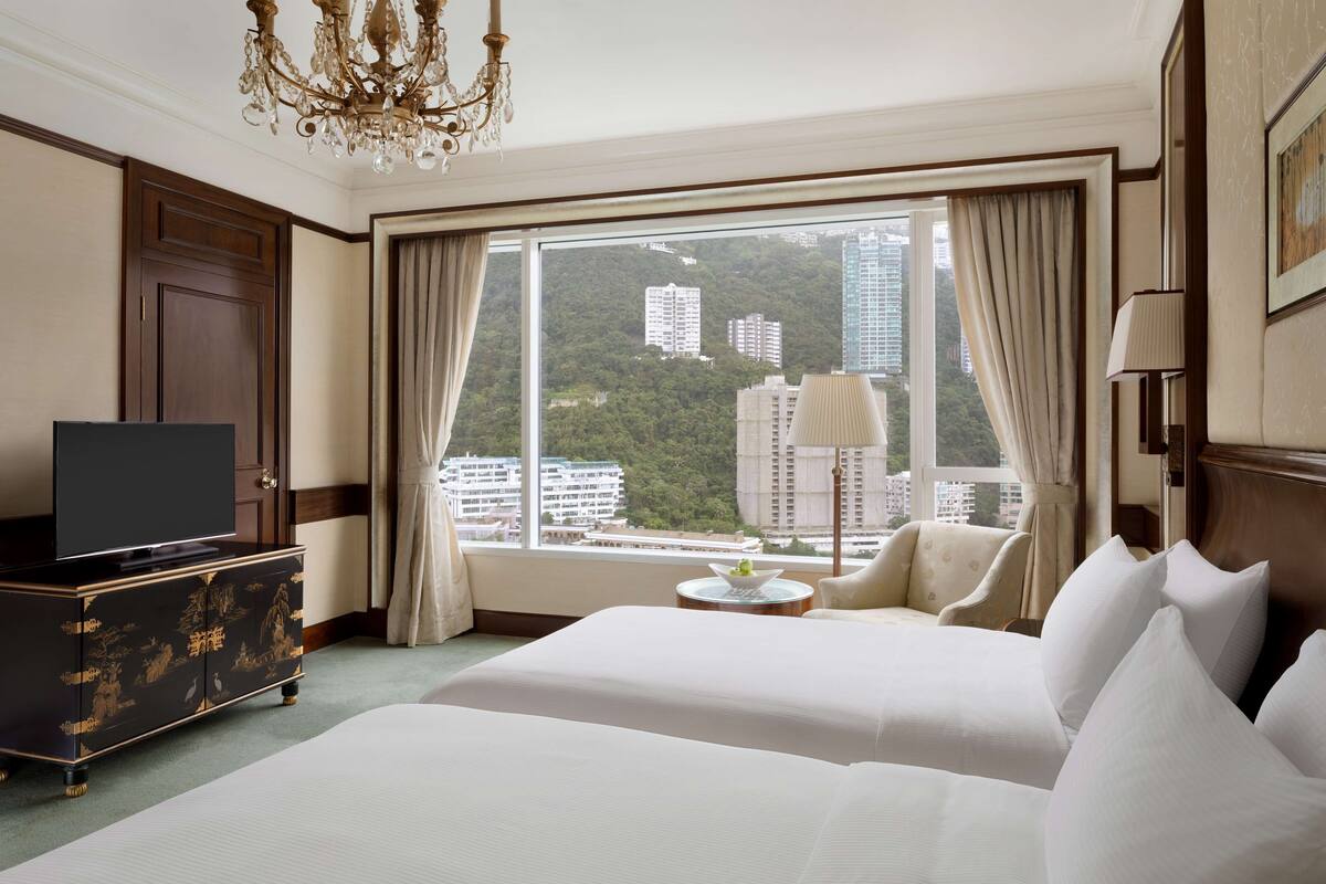 Quarto de hotel com uma cama grande, uma televisão sobre uma cômoda e vista para edifícios da cidade pela janela.