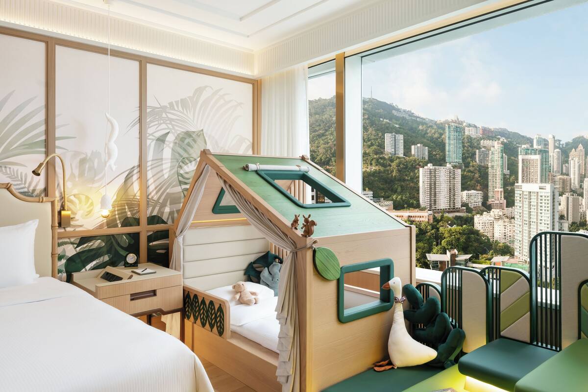 Quarto de hotel com uma cama, um pequeno parquinho, uma escrivaninha e vista para a paisagem urbana.