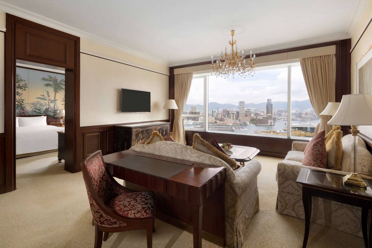 Quarto de hotel com mesa de jantar, sofá e uma ampla janela com vista para a cidade.