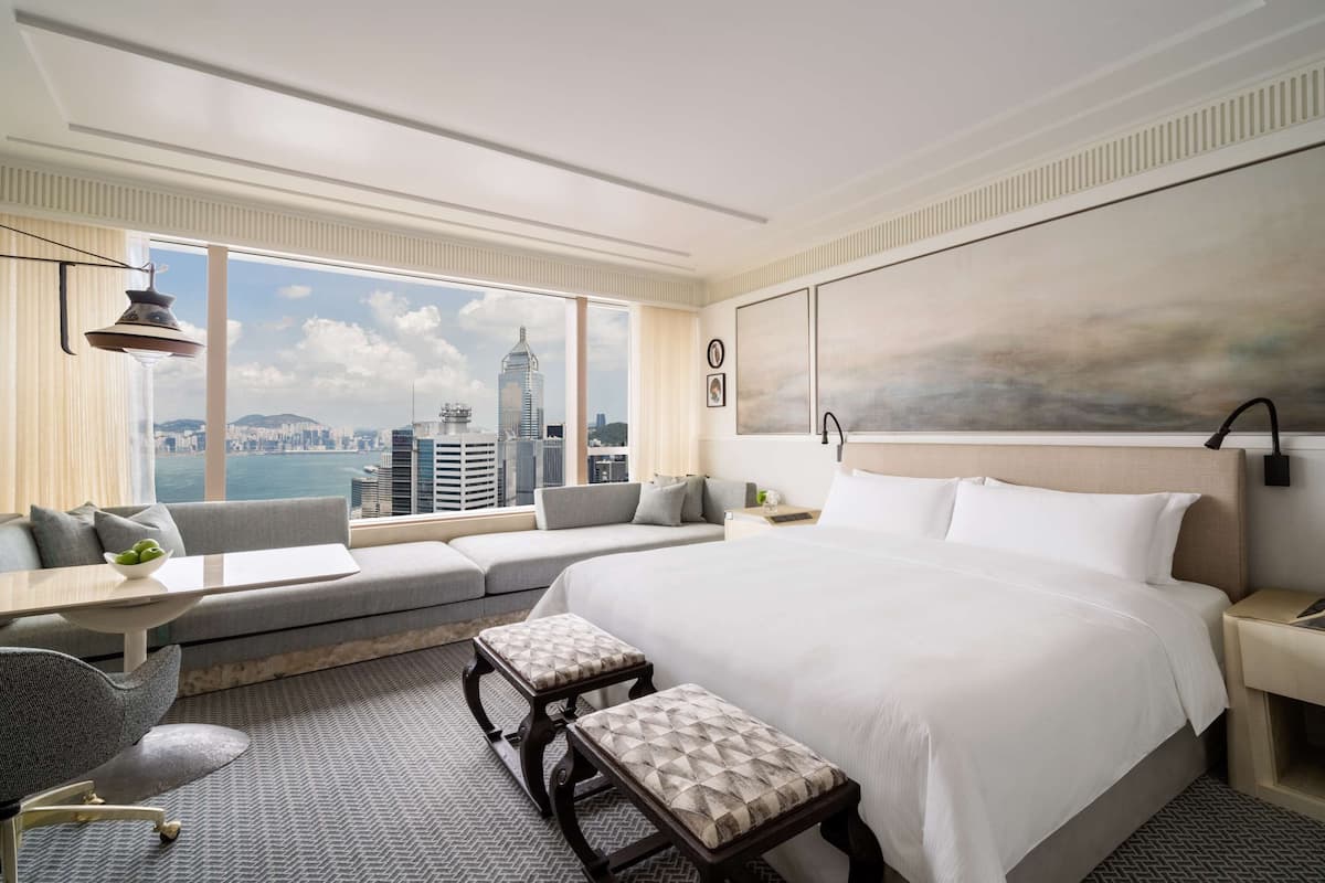 Quarto de hotel moderno com uma cama grande, um espaço de estar junto à janela e vista para a cidade.