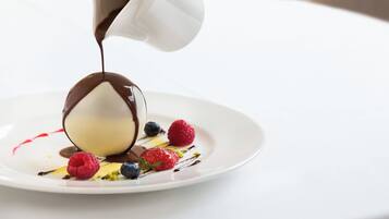 Sobremesa em um prato branco, com calda de chocolate sendo derramada, acompanhada de framboesas e amoras.