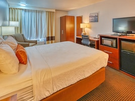 Quarto de hotel com uma cama grande, uma escrivaninha com computador, televisão e minibar.