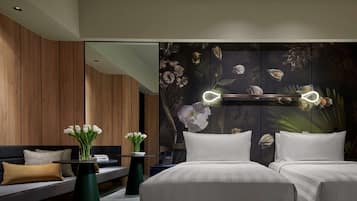 Quarto de hotel moderno com parede de painel de madeira, um espelho grande, uma cama com roupa de cama branca, uma mesa de cabeceira com telefone e um espaço de estar com almofadas e um vaso de flores.