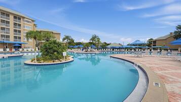 Piscina com espreguiçadeiras e guarda-sóis, cercada por um edifício com varandas.