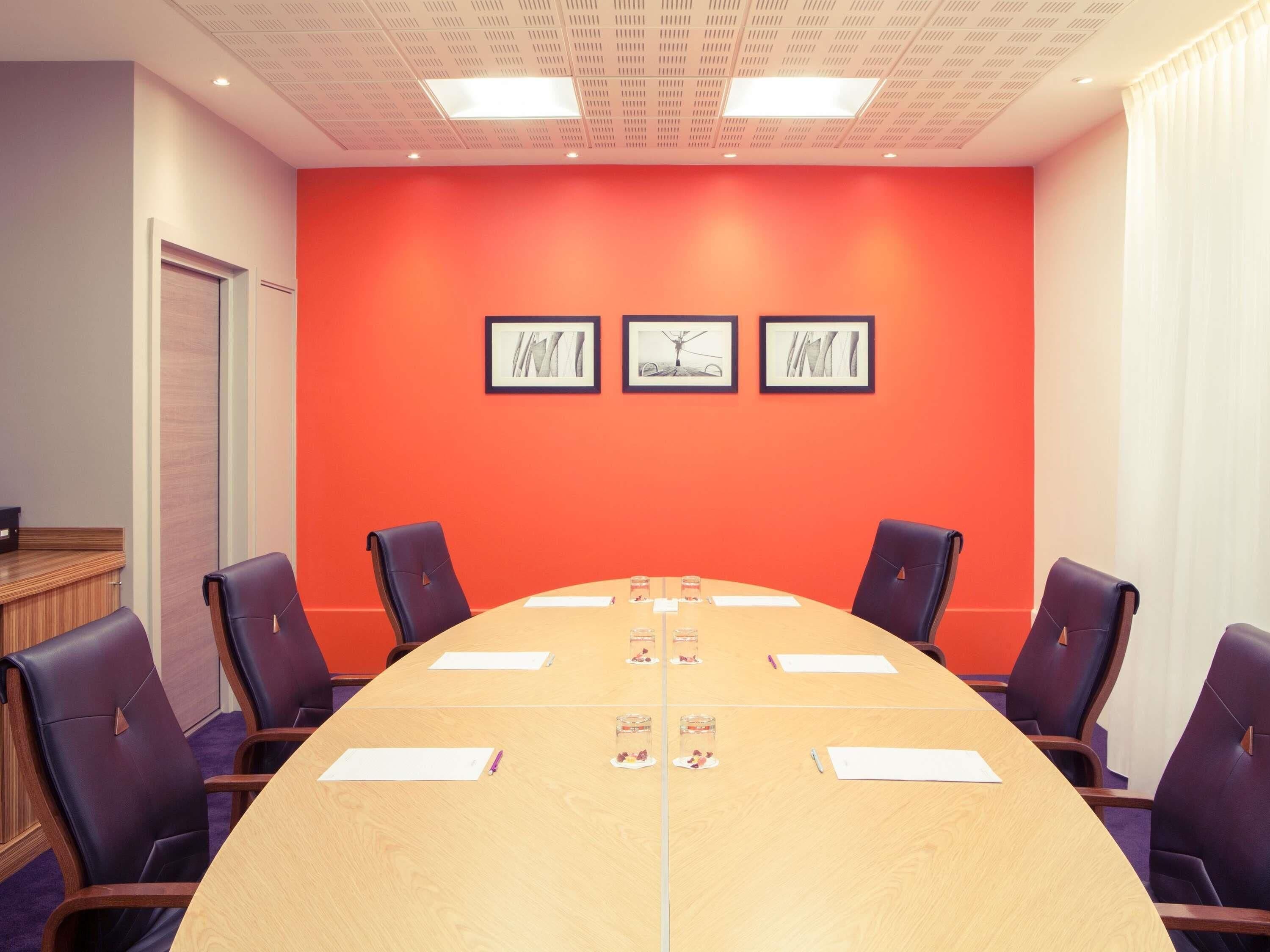 Uma sala de conferências com uma mesa redonda, seis cadeiras e três obras de arte emolduradas na parede.
