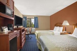 Quarto de hotel com uma secretária, televisão, duas camas, uma cadeira e uma janela com cortinas.