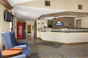 Um saguão com balcão de atendimento, um refrigerador de Coca-Cola, uma placa da Day's Inn e uma área de estar com cadeira e mesa.