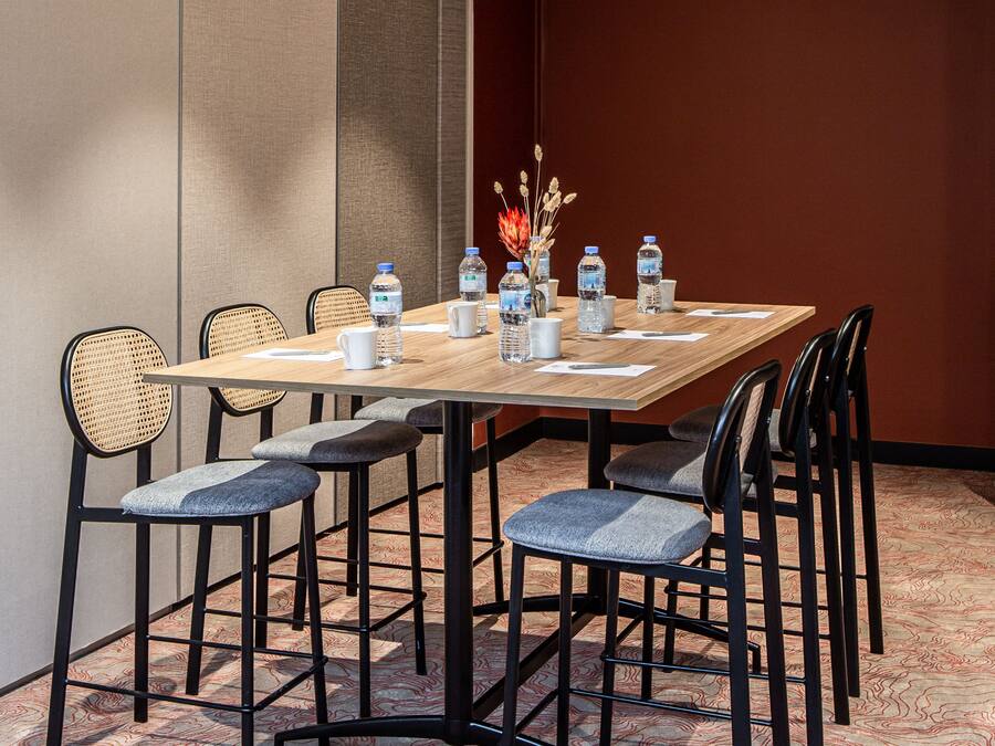 Uma sala de conferências com uma mesa de madeira, cadeiras pretas e garrafas de água.