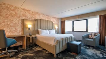 Quarto de hotel com cama, duas mesas de cabeceira, escrivaninha, cadeira e janela com cortinas.