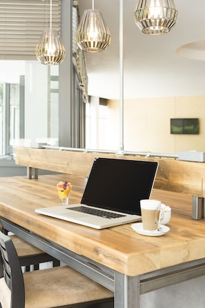 Uma mesa de madeira com um laptop, uma xícara de café e uma sobremesa.