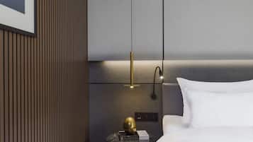 Quarto de hotel moderno com cama bem arrumada, mesa de cabeceira com abajur e painel de controle fixado na parede.