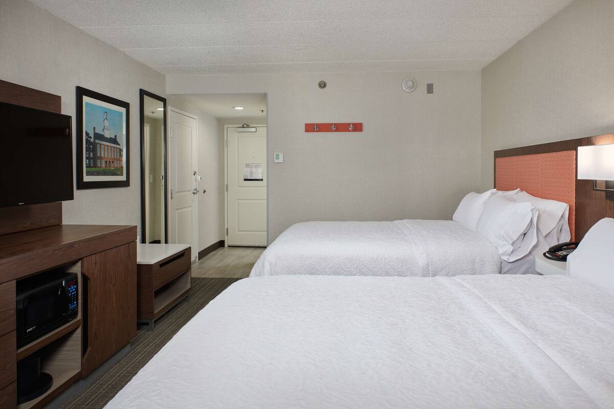 Quarto de hotel com duas camas, televisão, micro-ondas e espelho.