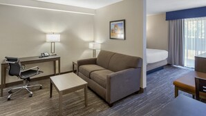 Quarto de hotel com cama, sofá, escrivaninha com cadeira, abajur e um quadro na parede.