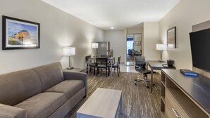 Quarto de hotel com sofá, escrivaninha com computador, televisão e área de refeições com cadeiras e mesa.