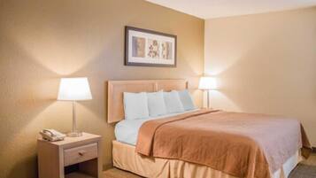 Quarto de hotel com cama, luminárias de cabeceira, mesa de cabeceira e quadro na parede.