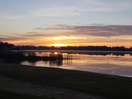 Um pôr do sol sobre um lago calmo, com uma construção pequena em primeiro plano.