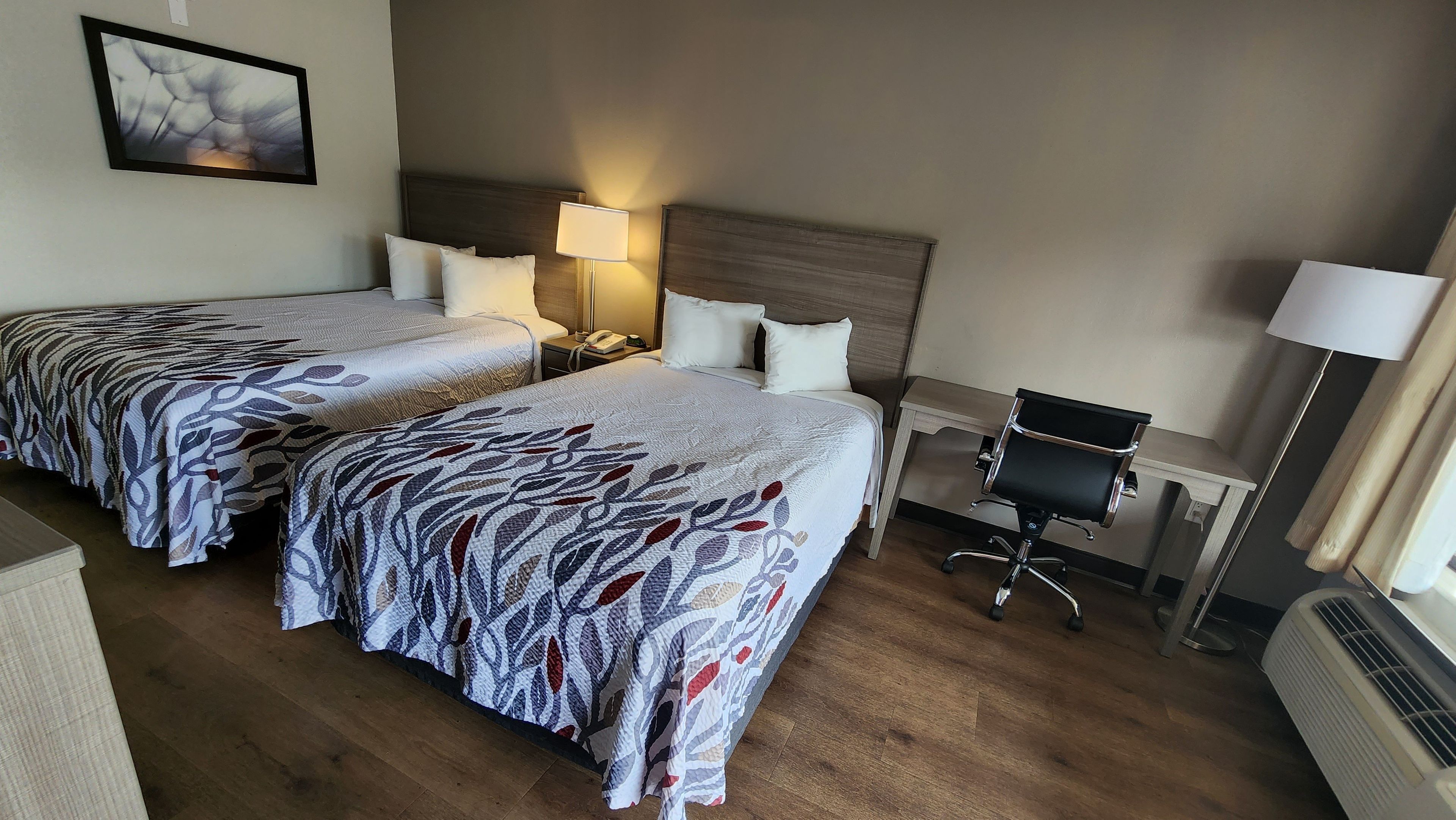 Quarto de hotel com duas camas, uma escrivaninha, uma cadeira, um abajur e um radiador.