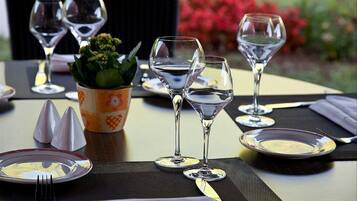 Mesa posta para refeição com copos de vinho, pratos e uma pequena planta em vaso.