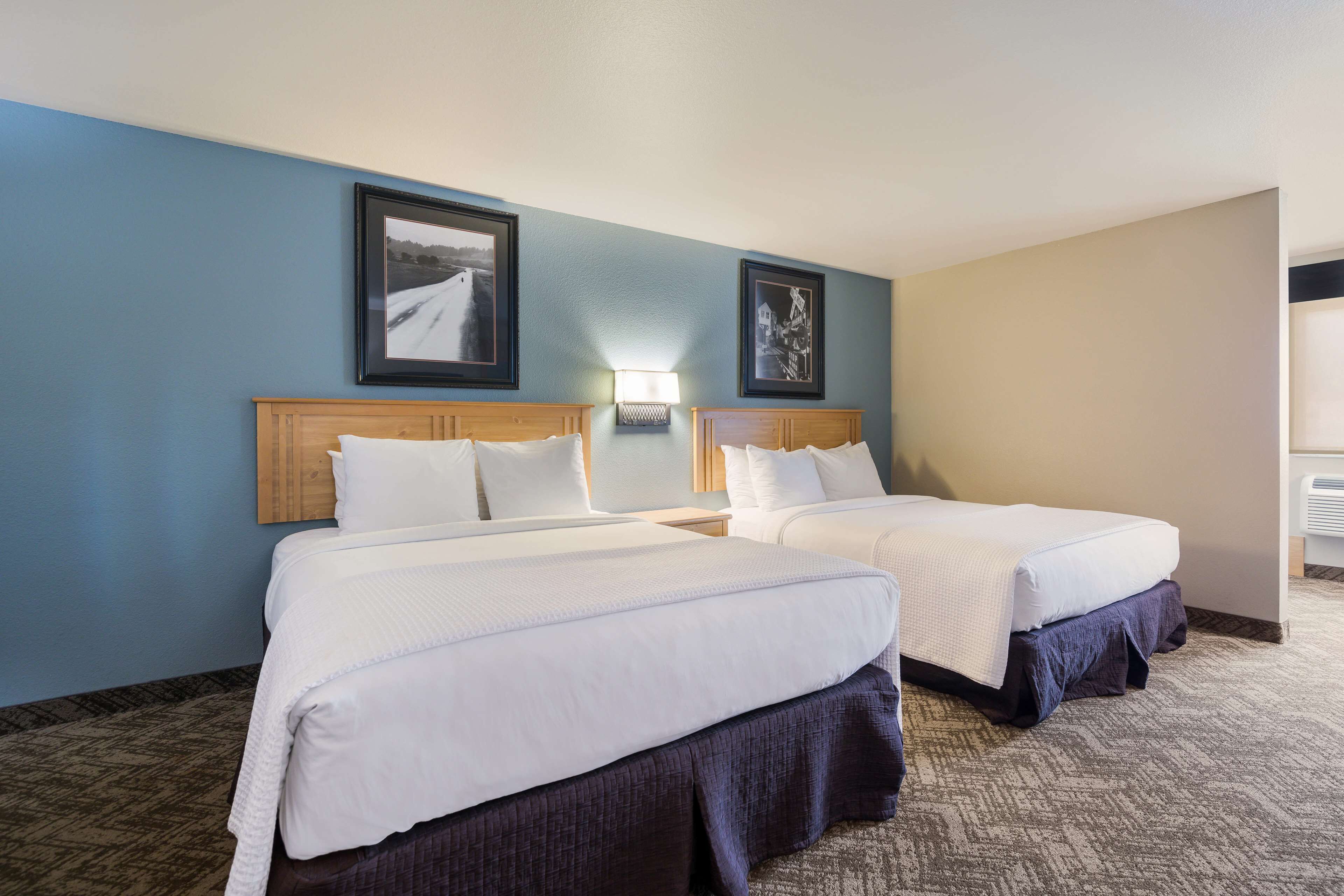 Quarto de hotel com duas camas, parede azul e quadros acima das camas.
