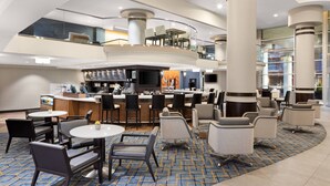 Um lobby de hotel moderno com área de bar, disposição de assentos e um mezanino.