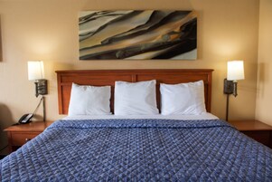 Quarto de hotel com uma cama grande, duas luminárias de cabeceira, um telefone e um quadro na parede.