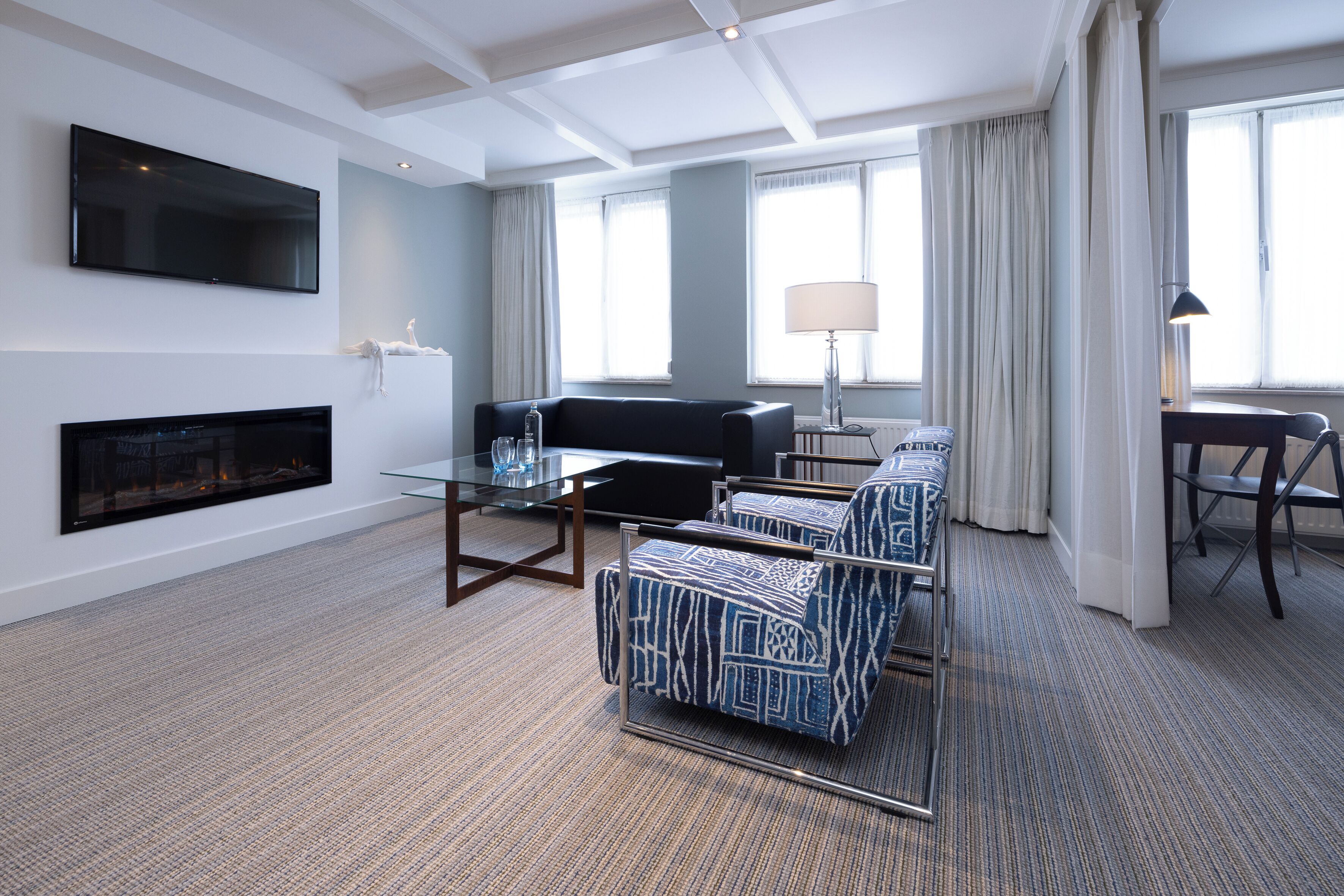 Quarto de hotel moderno com televisão de tela plana na parede, um conjunto de sofás, uma mesa de centro e uma lareira.
