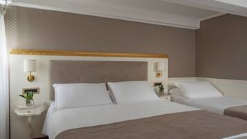 Quarto de hotel com duas camas, uma cabeceira grande, luminárias fixadas na parede e uma pequena mesa de cabeceira com uma planta.