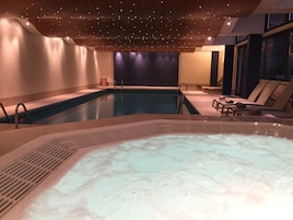 Piscina com hidromassagem, espreguiçadeiras e uma parede escura ao fundo.