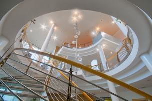 Um átrio com vários níveis, uma escadaria espiral central, guarda-corpos de vidro e um design arquitetônico moderno.