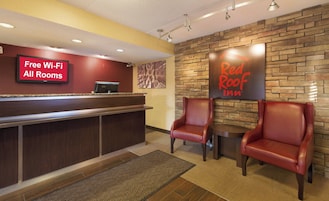 Área de recepção do Red Roof Inn com sinal digital indicando Wi-Fi gratuito, balcão de atendimento, duas poltronas de couro e parede de pedra ao fundo.