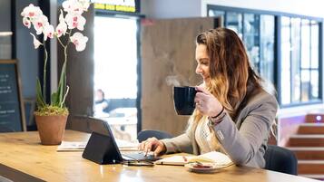 Uma pessoa trabalhando em uma mesa de madeira com um laptop, uma orquídea em vaso e uma caneca de café.