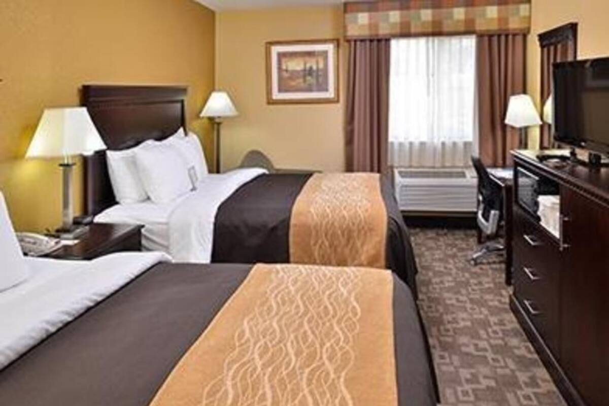 Quarto de hotel com duas camas, uma escrivaninha, televisão e uma janela com cortinas.