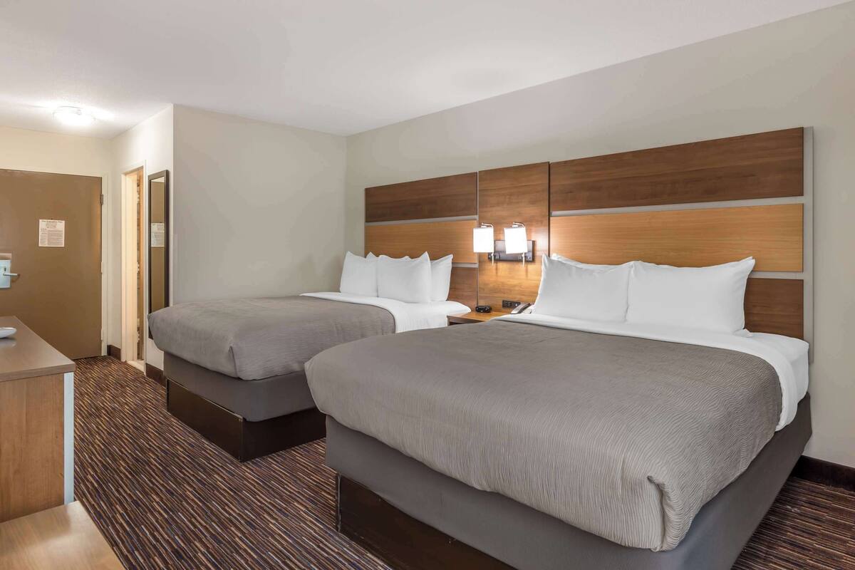 Quarto de hotel com duas camas, uma escrivaninha e um espelho.