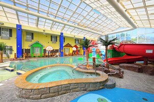 Piscina interna com hidromassagem, toboáguas e tema tropical.