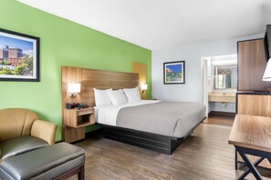 Quarto de hotel com cama, escrivaninha, cadeira e televisão.