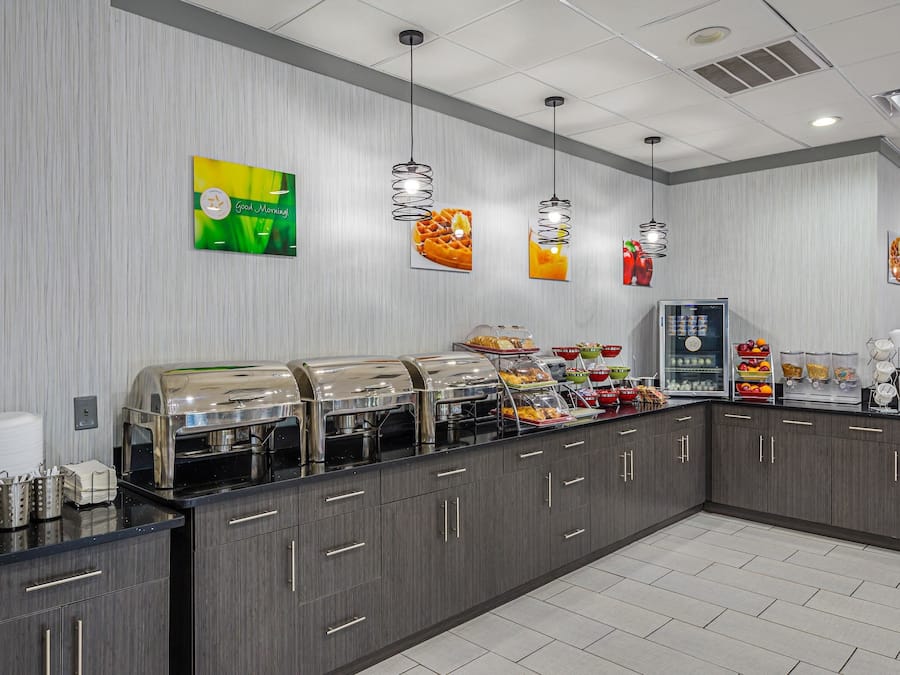Uma mesa de buffet com vários distribuidores de comida, um espaço para café e uma geladeira.
