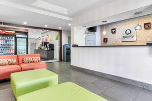 Uma área de recepção com um refrigerador Coca-Cola, um balcão com a inscrição 'Quality' e assentos com almofadas coloridas.