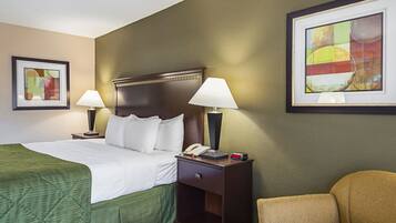 Quarto de hotel com cama, duas luminárias de cabeceira, mesa de cabeceira com telefone e relógio, e uma cadeira.