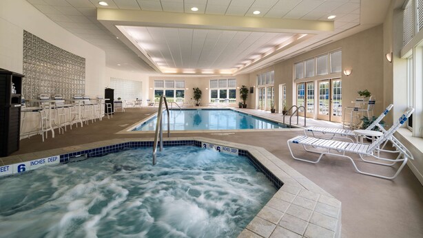 Piscina interna com espreguiçadeiras, hidromassagem e área de estar com mesas e cadeiras.