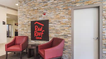 Placa da Red Roof Inn em uma parede de pedra texturizada, duas poltronas de couro vermelho, uma mesa redonda pequena e uma porta.