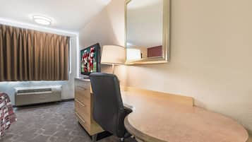 Quarto de hotel com escrivaninha, cadeira, televisão, luminária e um espelho grande.