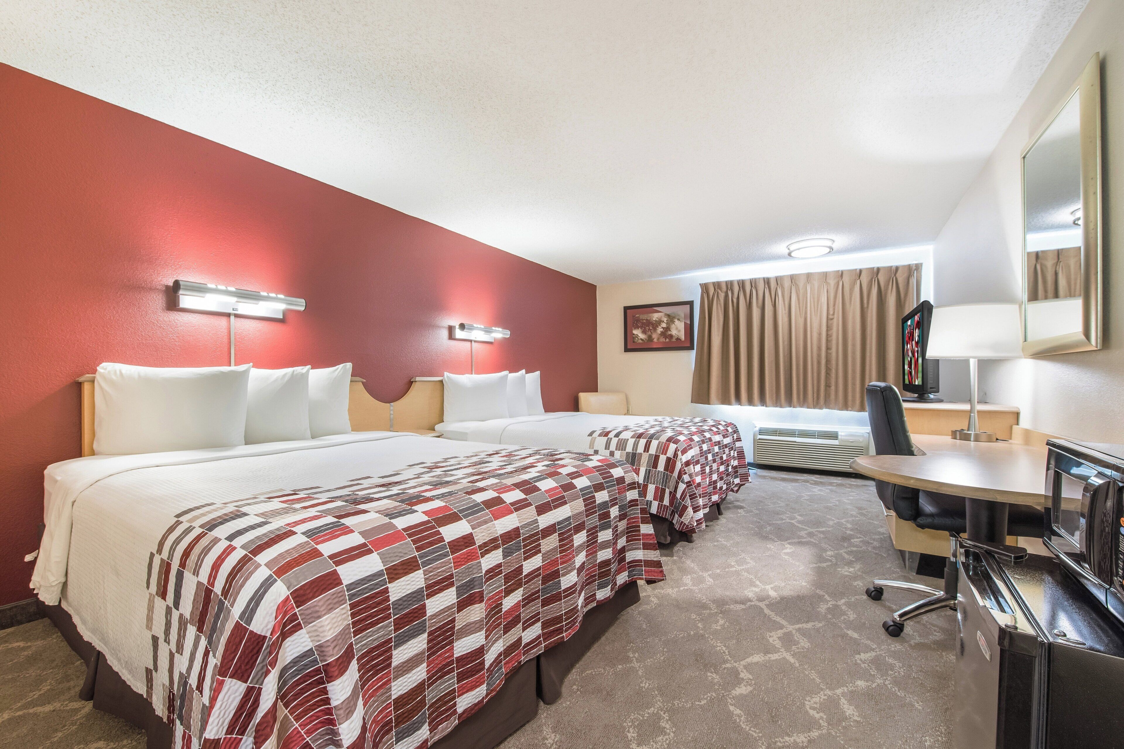 Quarto de hotel com duas camas, uma escrivaninha, uma cadeira, uma televisão e um espelho.