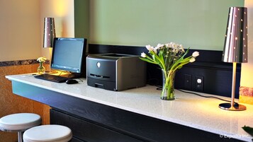 Uma mesa de recepção com um computador, impressora e um vaso de flores.