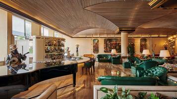Um hall amplo com piano, sofás verdes, área de bar e um espelho grande.
