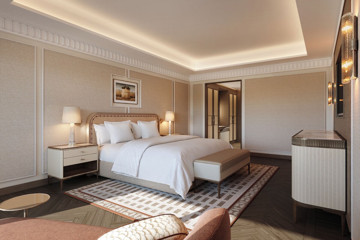Quarto de hotel moderno com uma cama grande, mesas de cabeceira, escrivaninha e uma cadeira.
