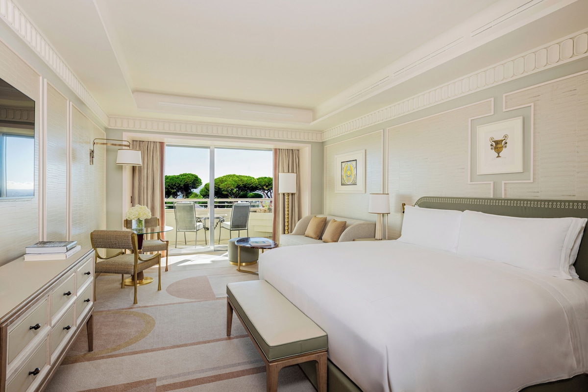 Quarto de hotel com uma cama grande, escrivaninha, cadeira e vista para o exterior.