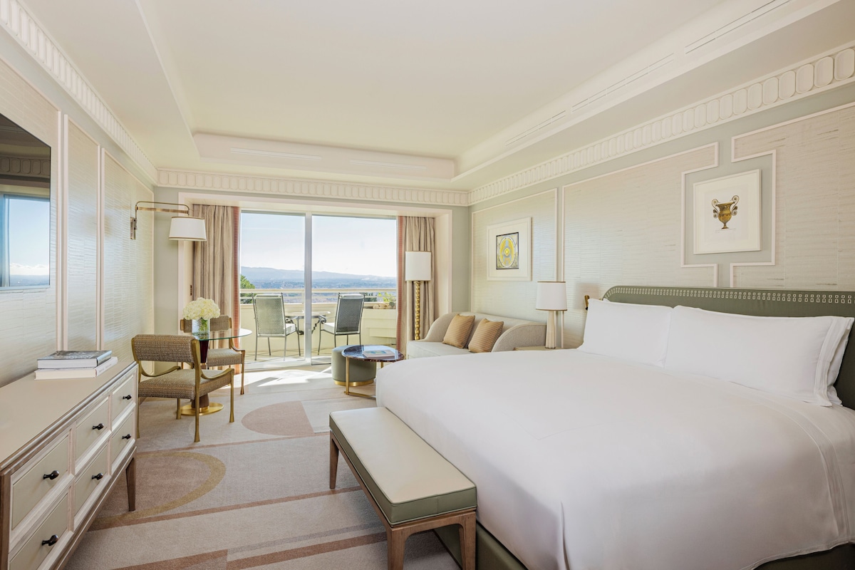 Quarto de hotel com uma cama grande, uma escrivaninha, uma cadeira e vista para o exterior.