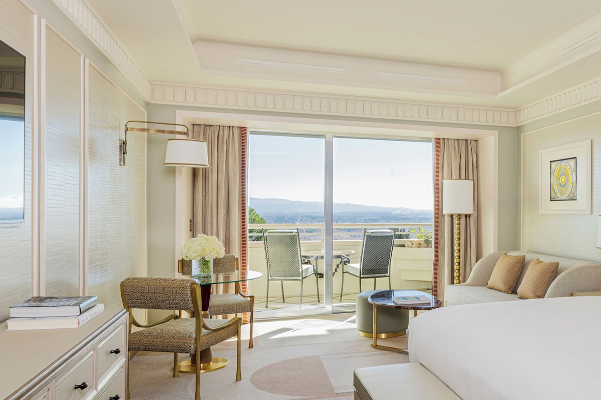 Quarto de hotel com varanda, cama, escrivaninha e cadeira.